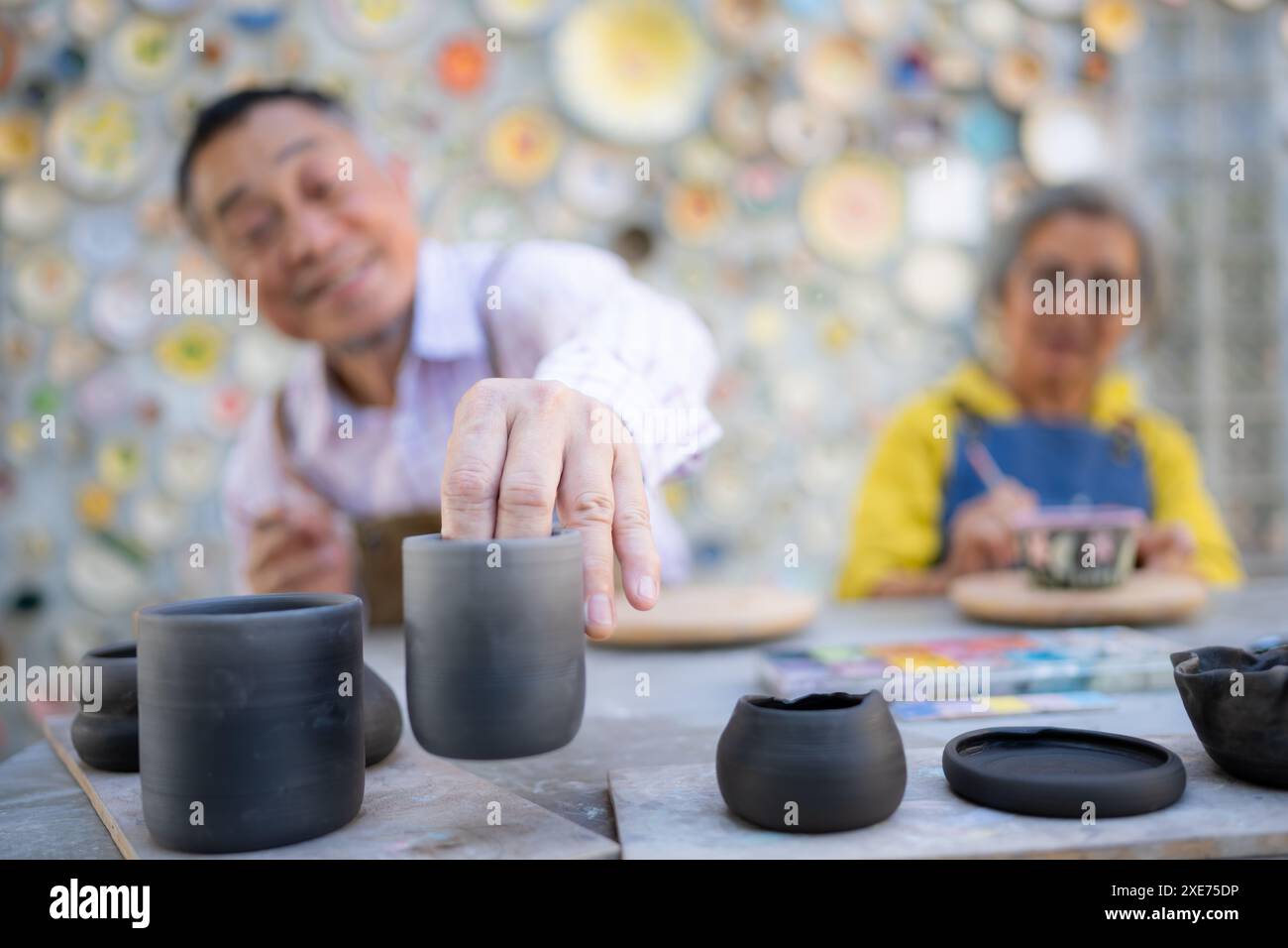 In the pottery workshop, an Asian retired couple is engaged in pottery ...