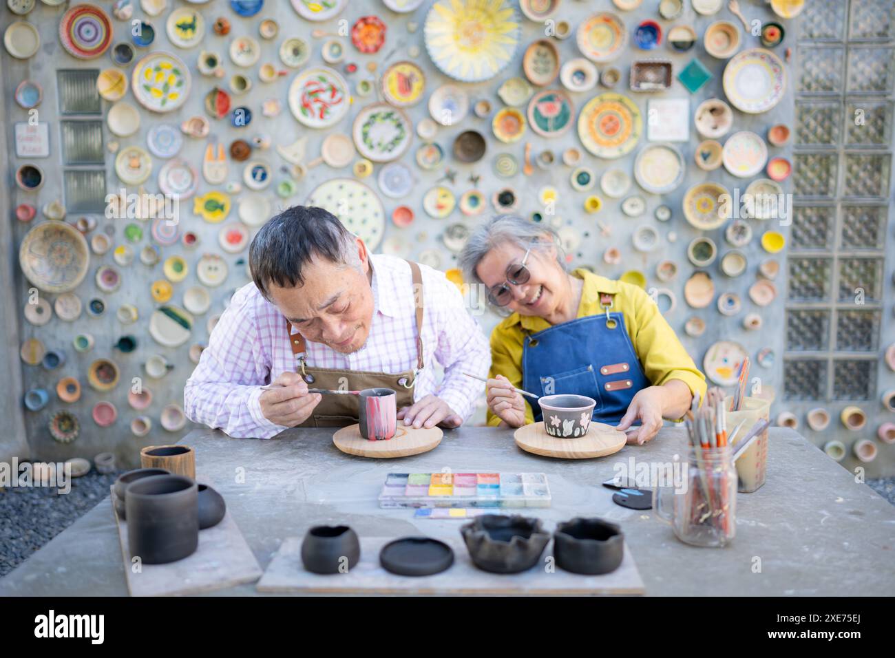 In the pottery workshop, an Asian retired couple is engaged in pottery ...