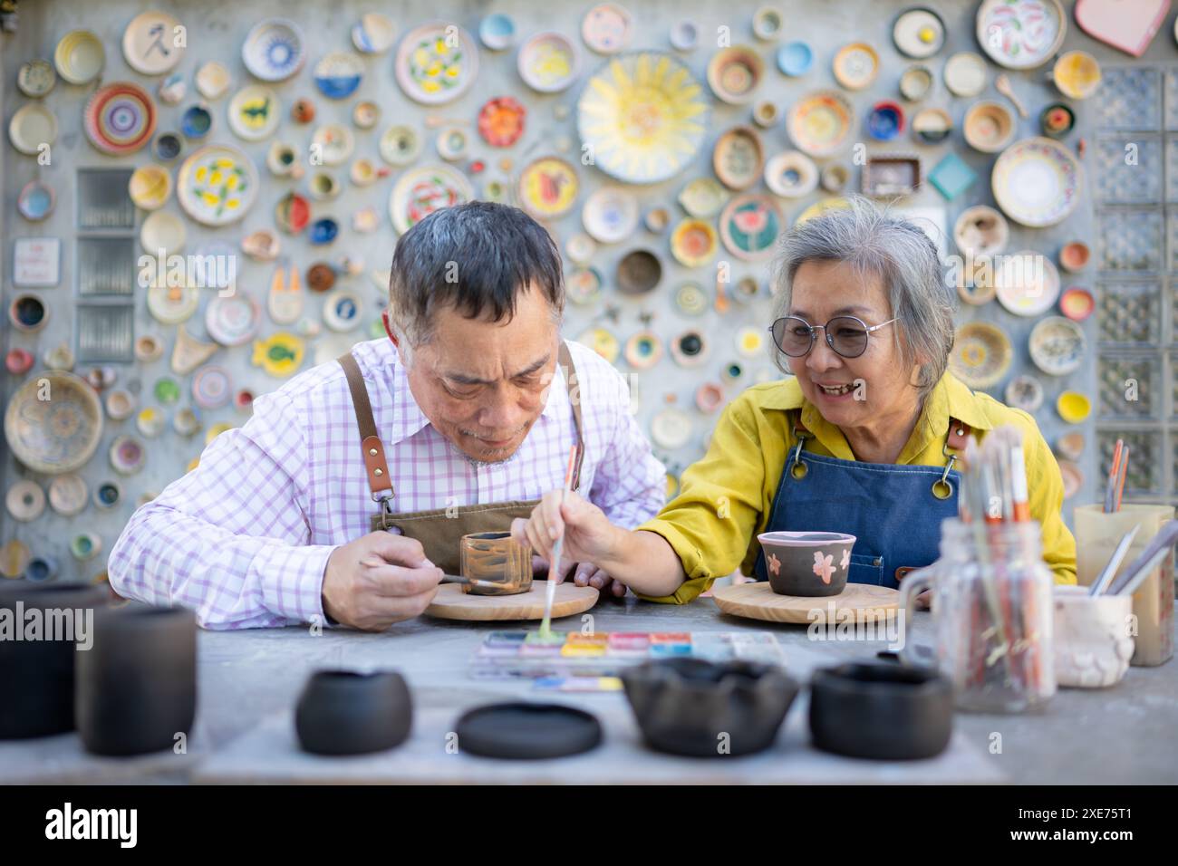 In the pottery workshop, an Asian retired couple is engaged in pottery ...