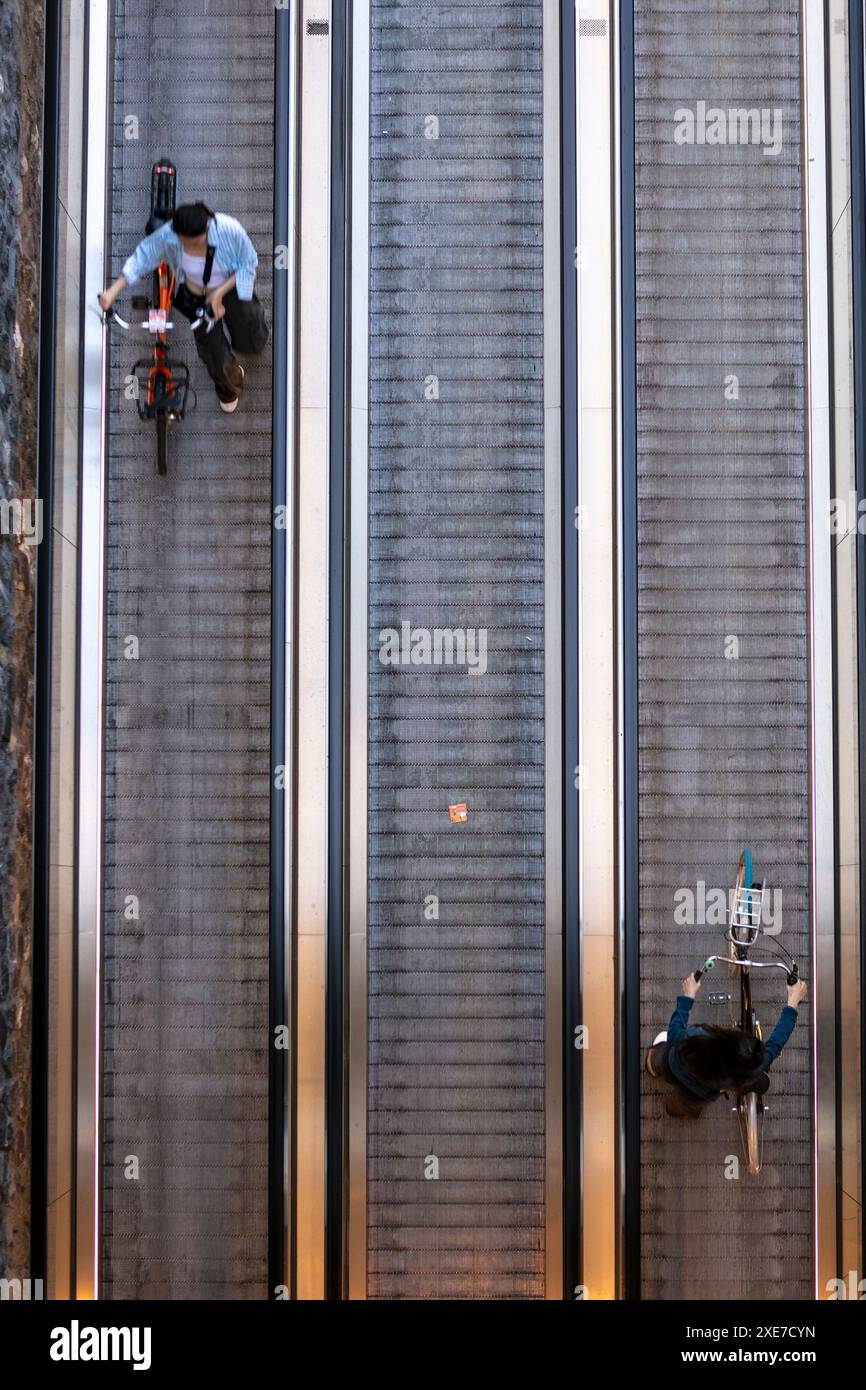 An overhead view of two women pushing their bicycles on a travelator ...