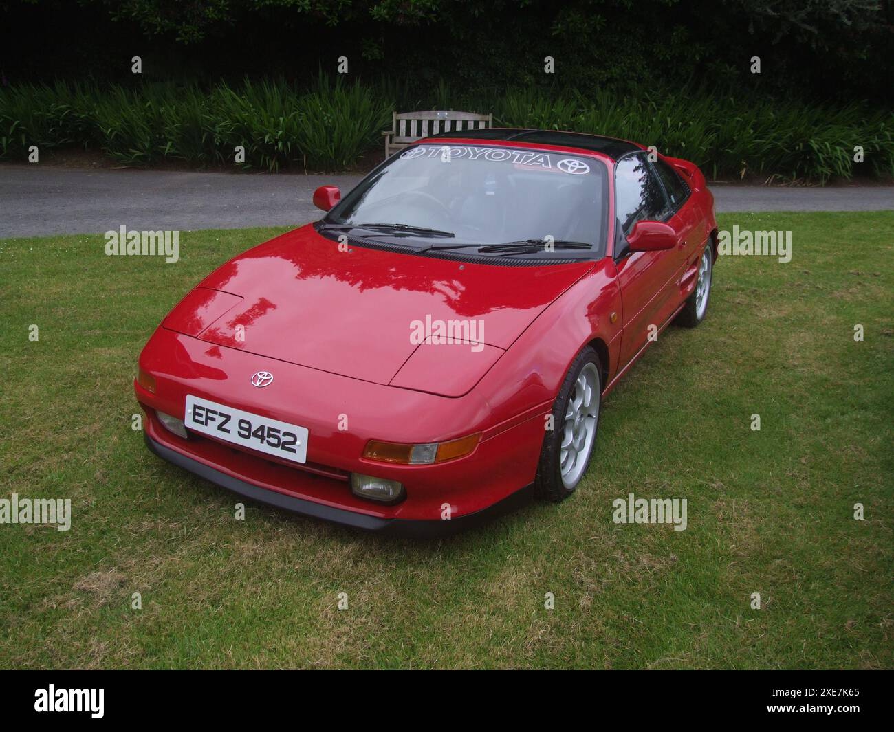Red Toyota MR2 sports car parked on a lawn with greenery in the ...