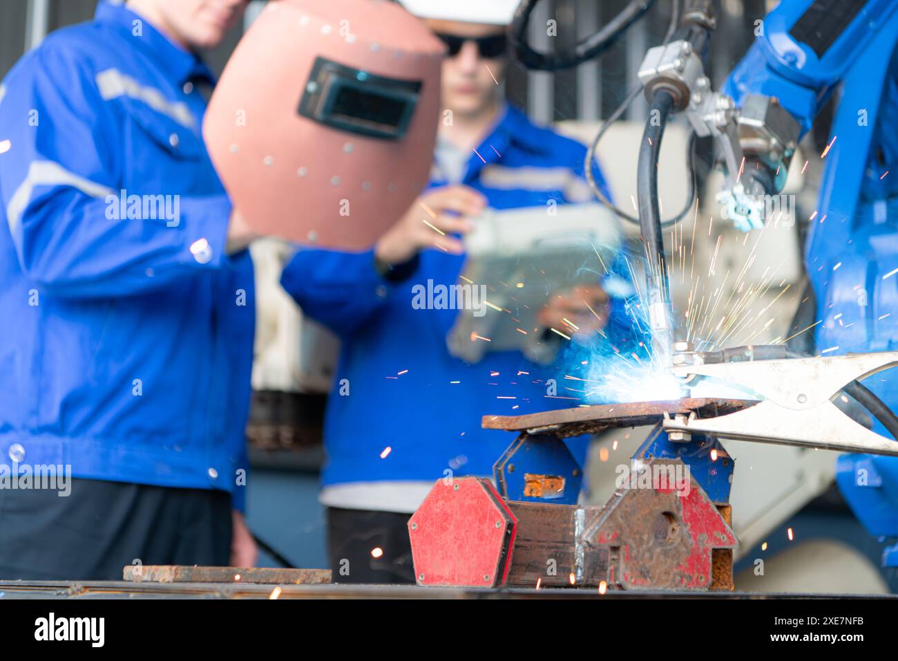 Industrial workers working with robotic arm welding machine in factory ...