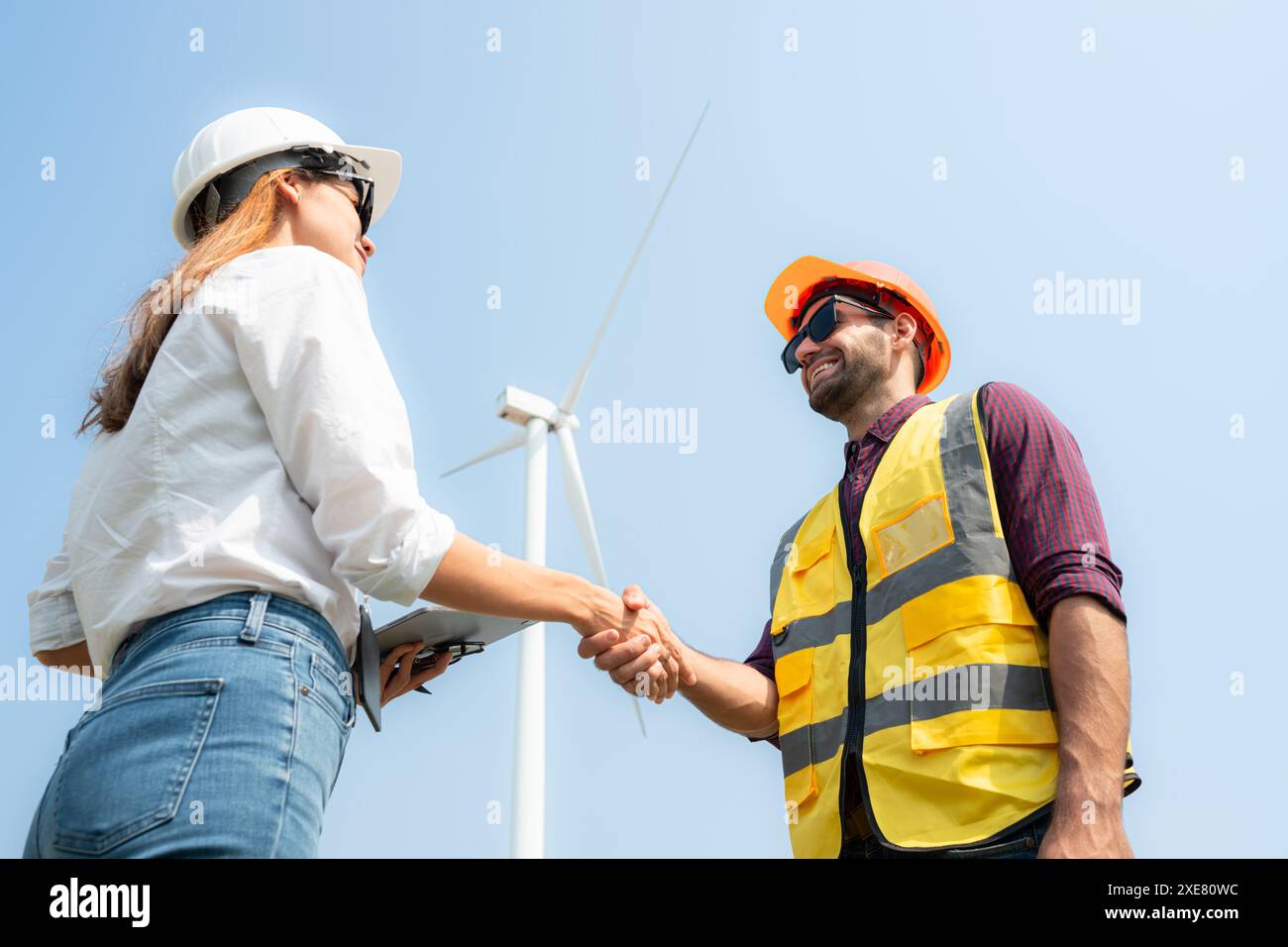 Engineer and technician shaking hands with wind turbine on the ...