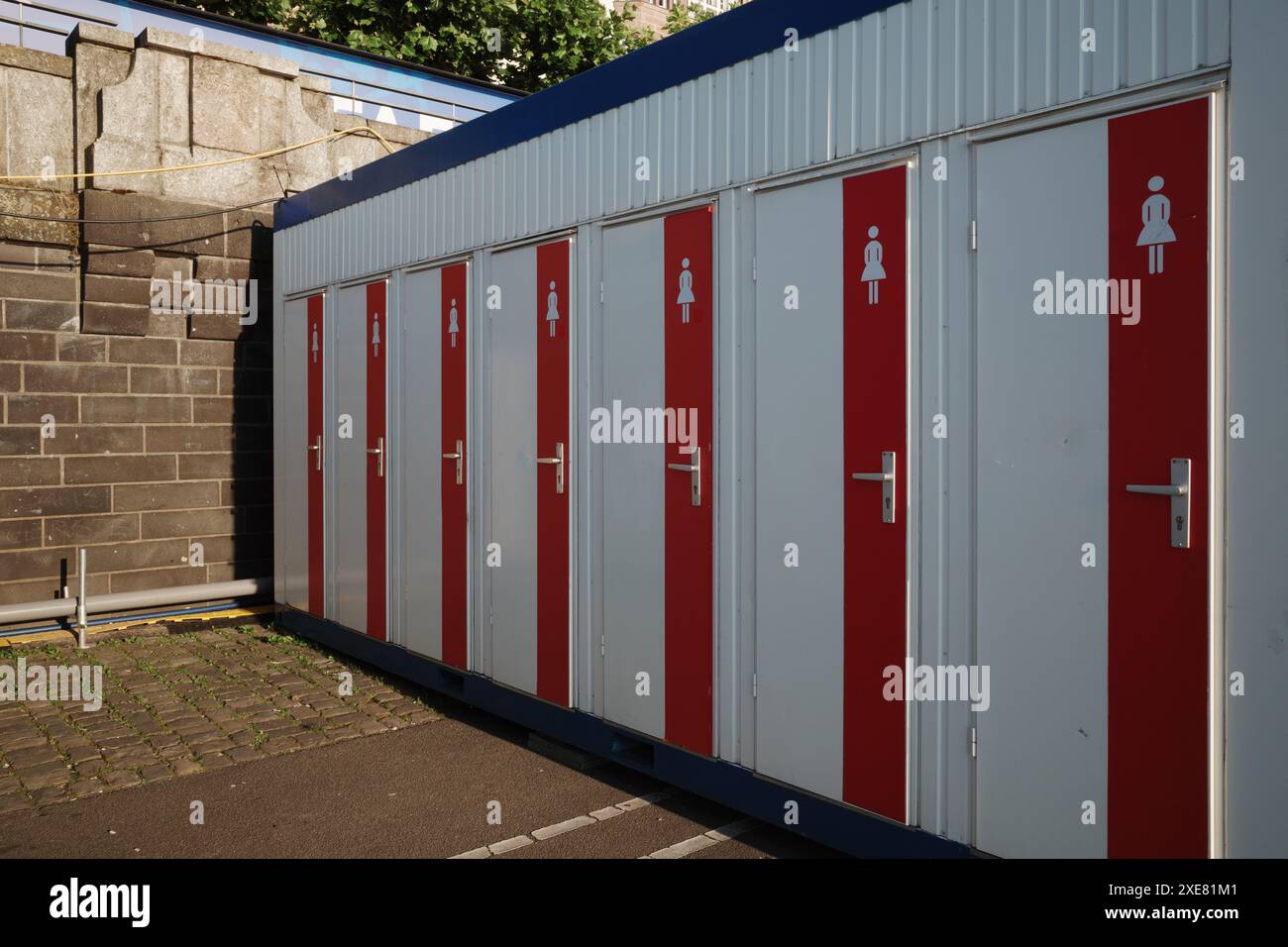 A row of portable restroom cabins, each with a red and white door ...