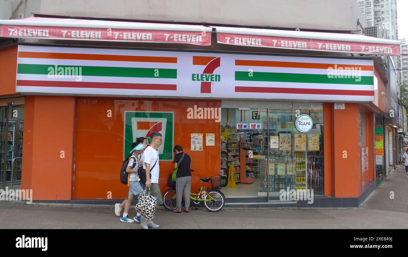 Pedestrian walks past the american convenience store, 7-Eleven logo and store in Hong Kong ...
