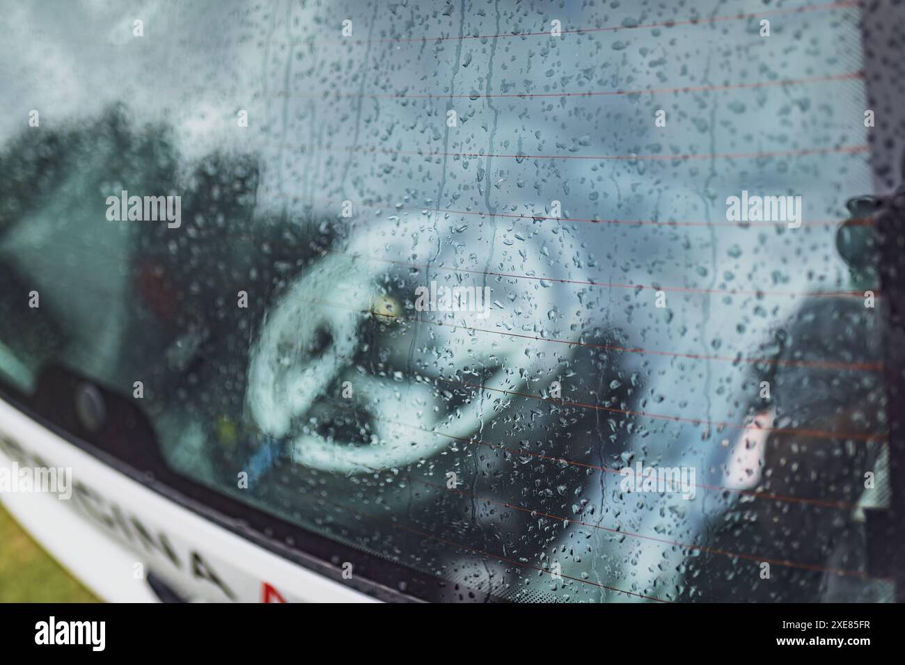 Close-up of rain drops on a rally car rear window with reflections of ...
