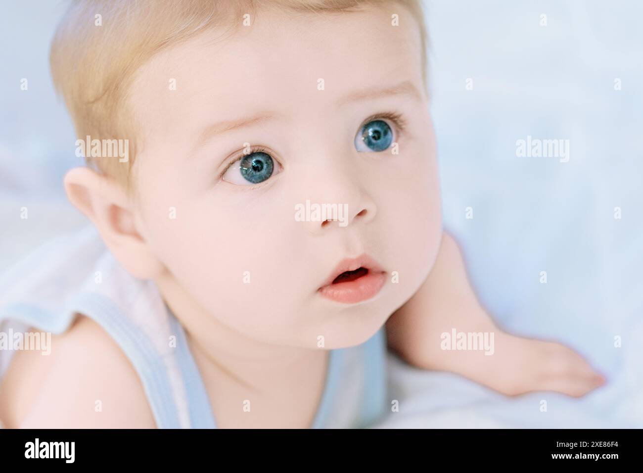 Beautiful baby with big blue eyes is lying on his stomach on a soft ...