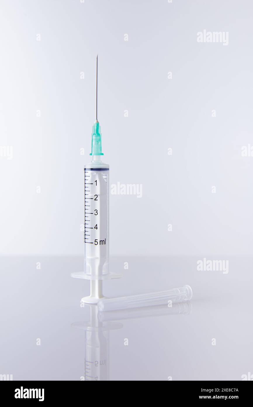 Close-up of a vertical syringe with its cap on the table. White ...
