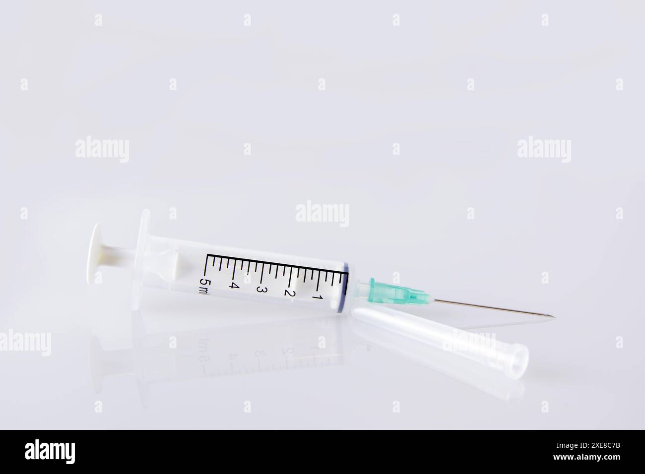 Medical syringe with its needle and cap removed, it is lying on white ...
