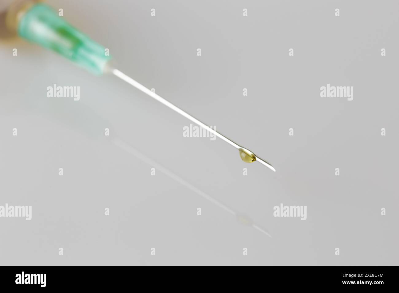 Close-up of the needle of a syringe, with a drop on the needle. Grey ...