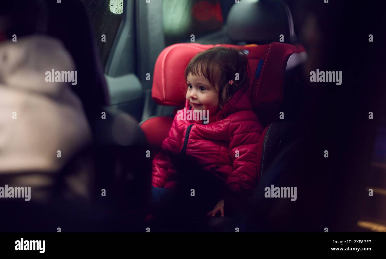A young girl sits comfortably in a modern car seat, secured and ready ...