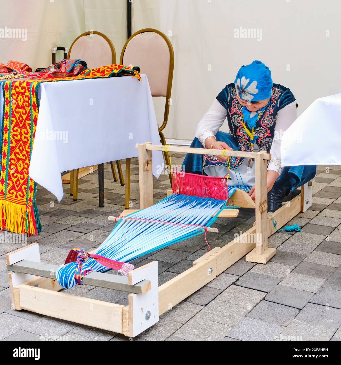 Asian woman weaving wicker runner from colorful wool threads on hand ...