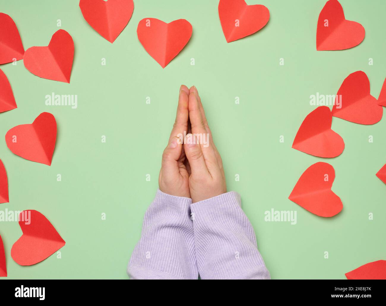 Woman's hands folded in a prayer pose on a green background with red ...
