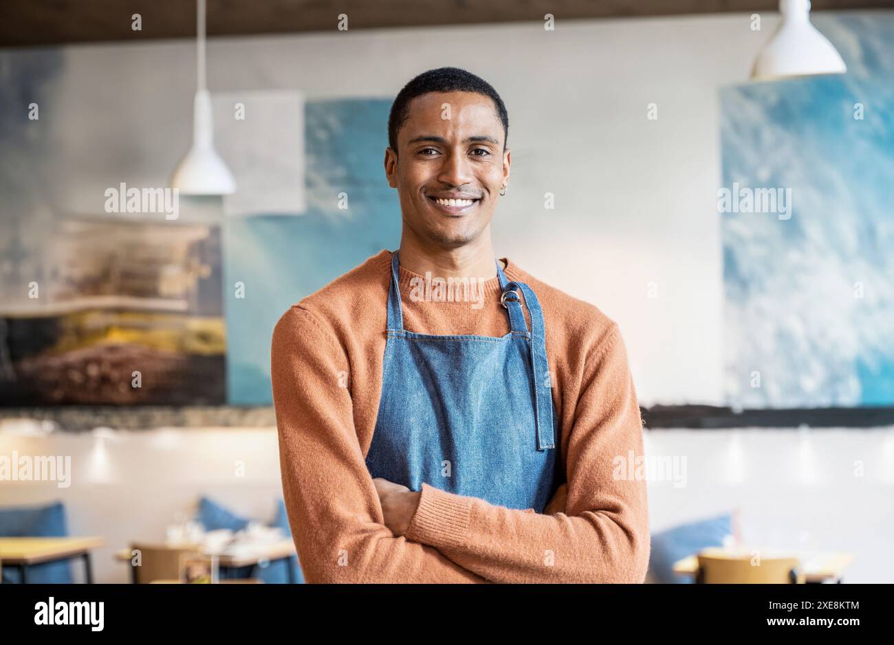 Smiling moroccan young man wearing a casual apron in a modern café. He ...