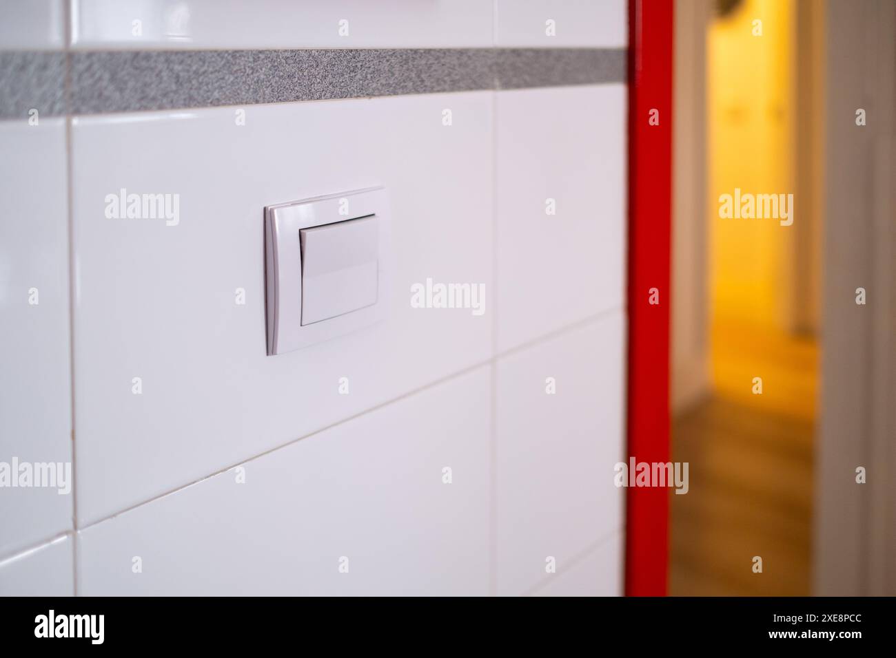Detail of a white light switch on the tile wall of a kitchen. There is ...