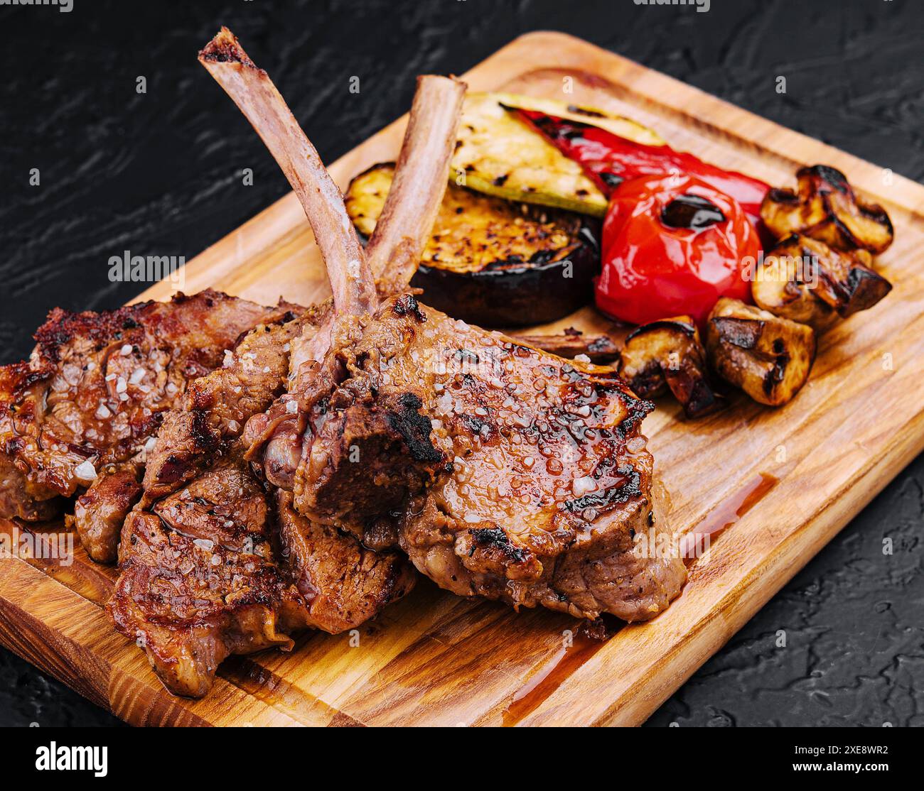 Tasty grilled lamb ribs with vegetables on board Stock Photo - Alamy