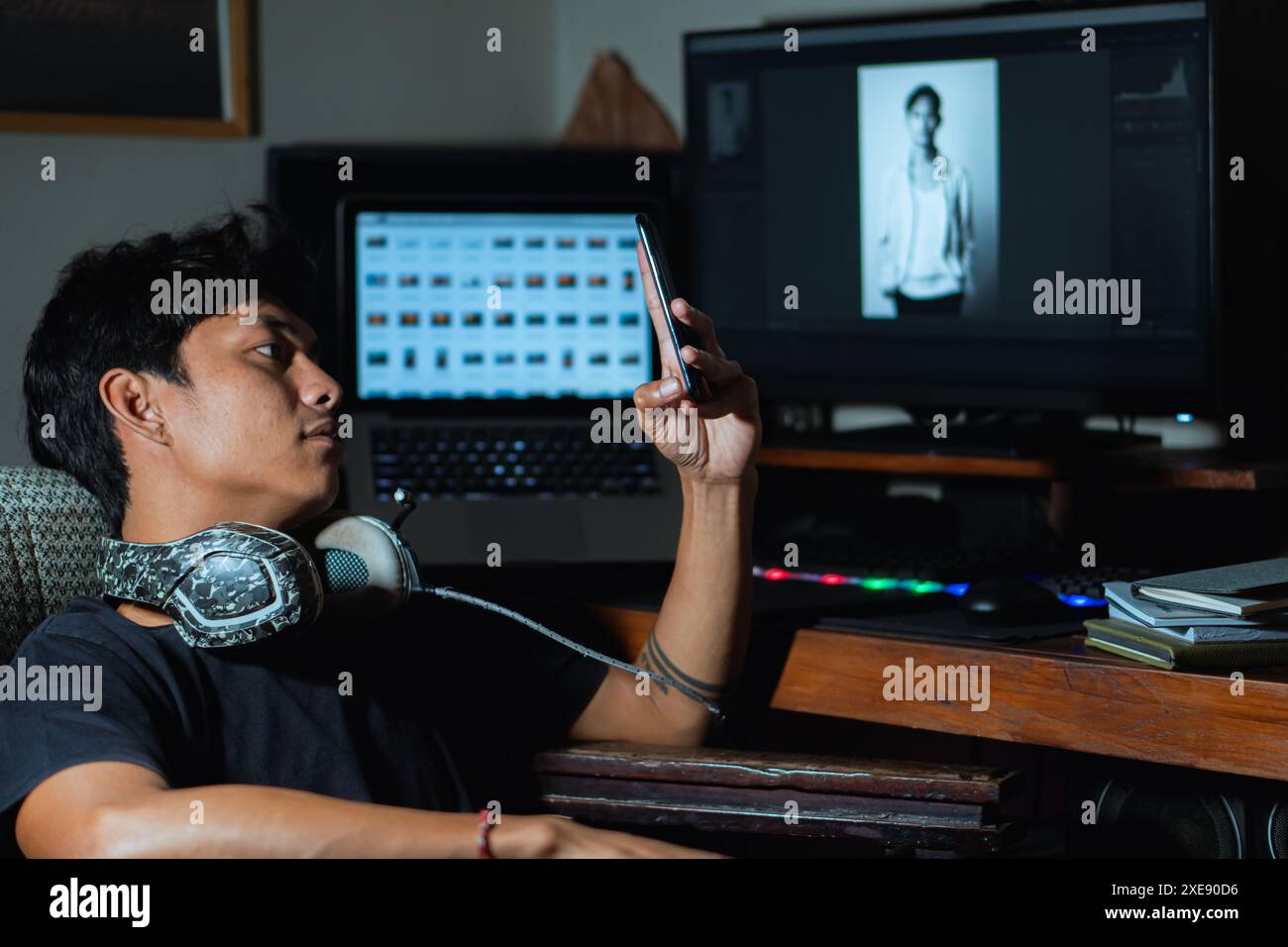 Young man sitting at a desk with headphones around his neck, looking at ...