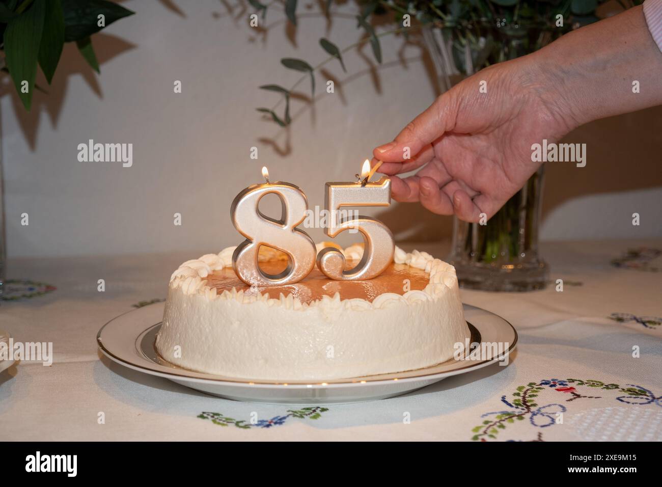 An adult hand lights birthday candles with the number 85 on a nice ...