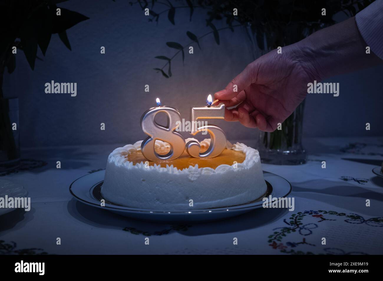 An adult hand lights birthday candles with the number 85 on a nice ...