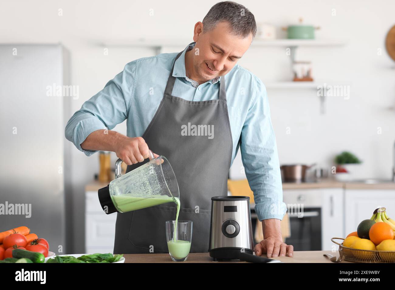 Mature man pouring fresh smoothie from blender into glass in kitchen ...