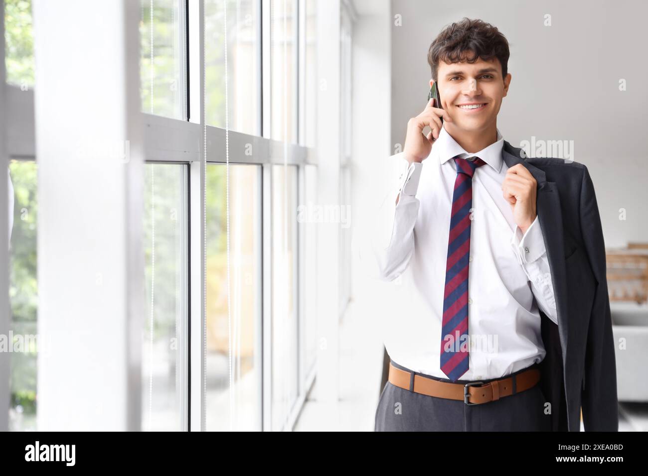 Male accountant talking with mobile phone and holding jacket in office ...