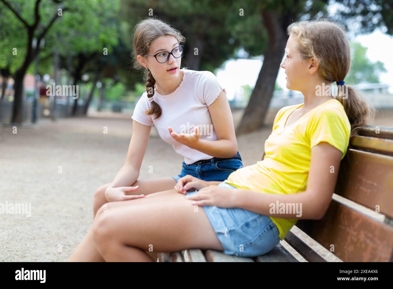 Two friendly young girls sitting on bench Stock Photo - Alamy