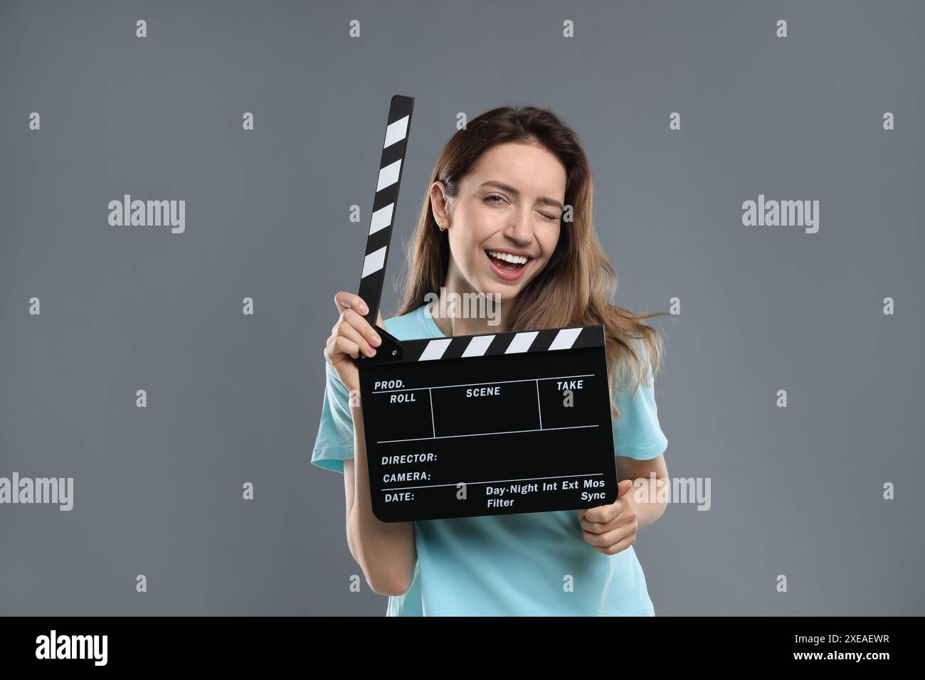 Making movie. Smiling woman with clapperboard winking on grey ...