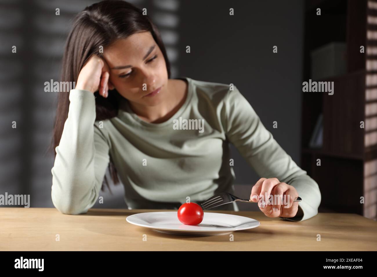 Eating disorder. Sad woman with fork near tomato at wooden table Stock ...