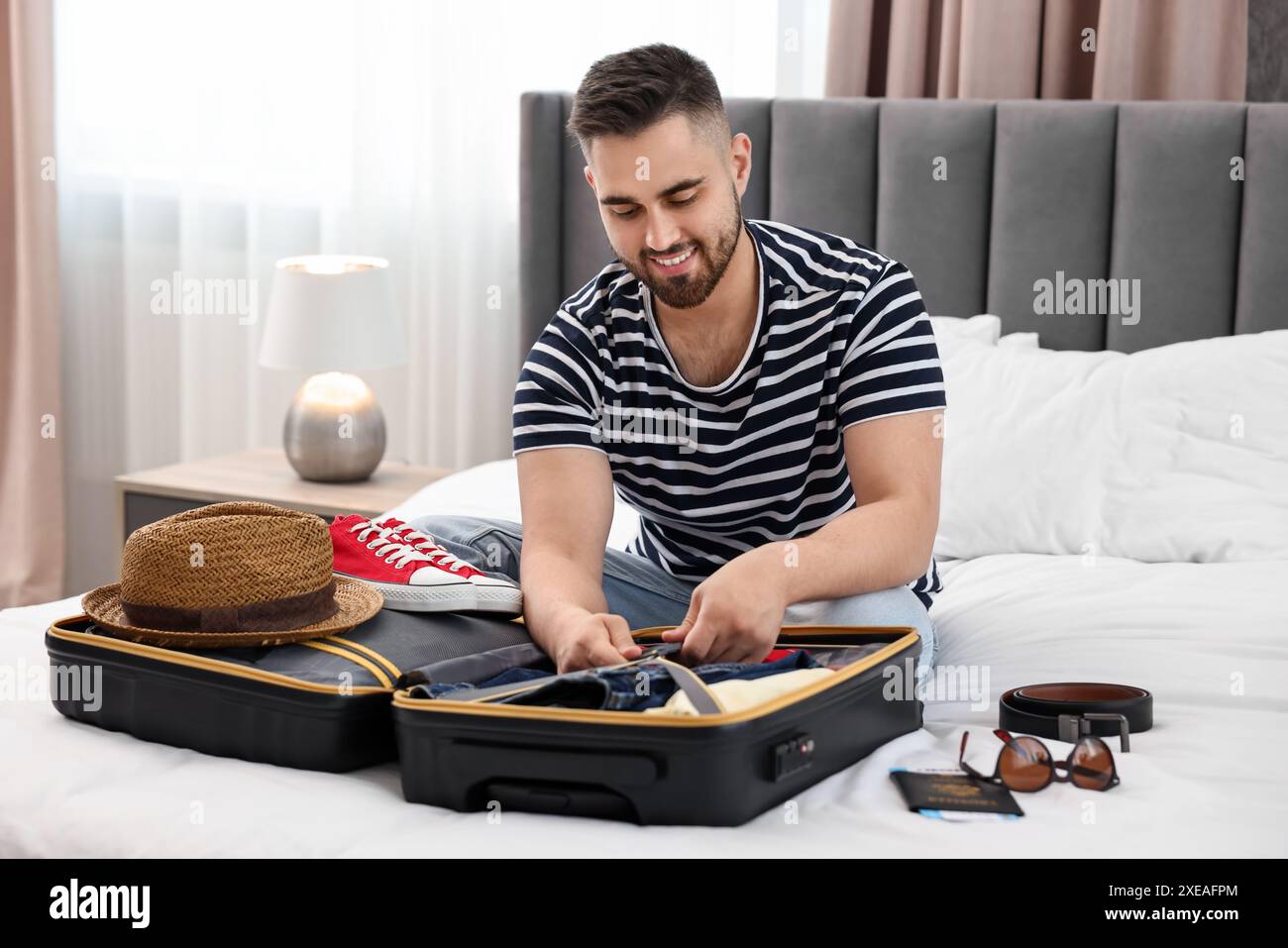 Man packing suitcase for trip on bed indoors Stock Photo - Alamy