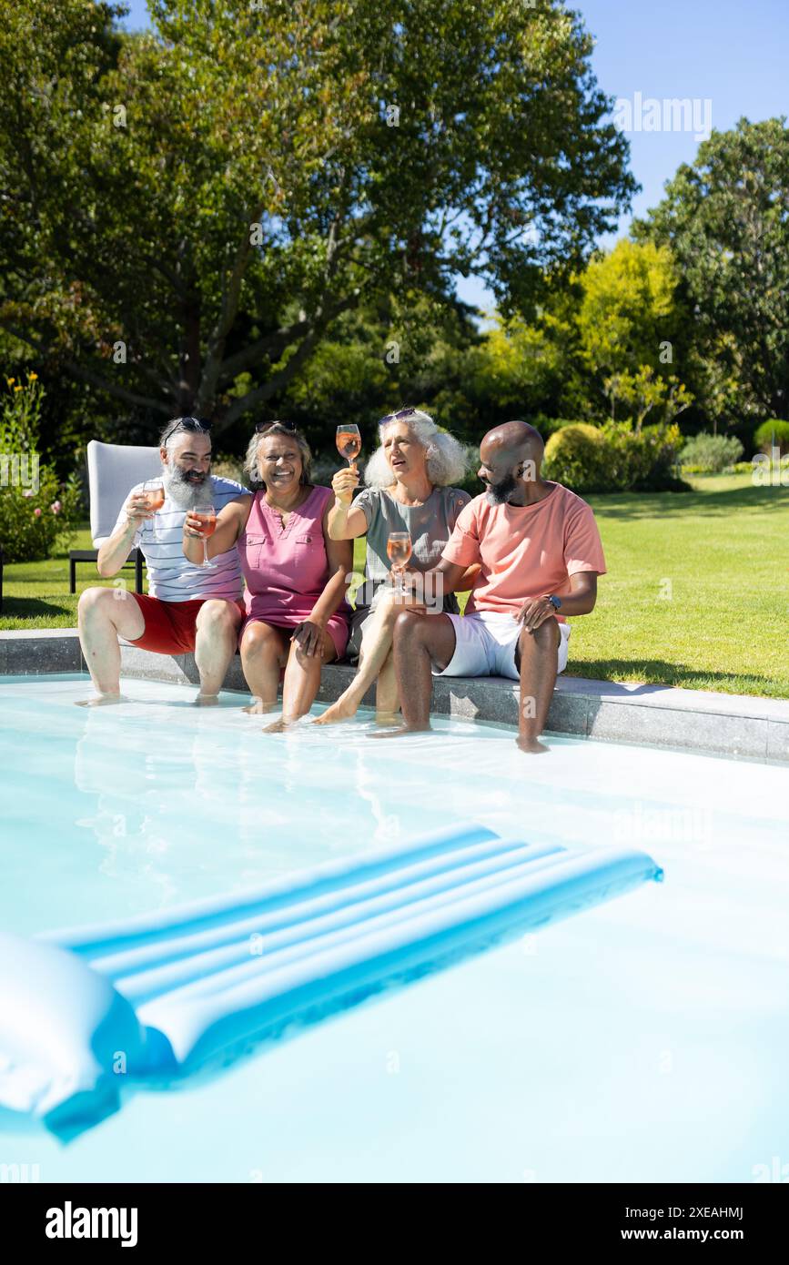 Toasting with drinks, diverse group of senior friends sitting by pool, enjoying summer Stock ...