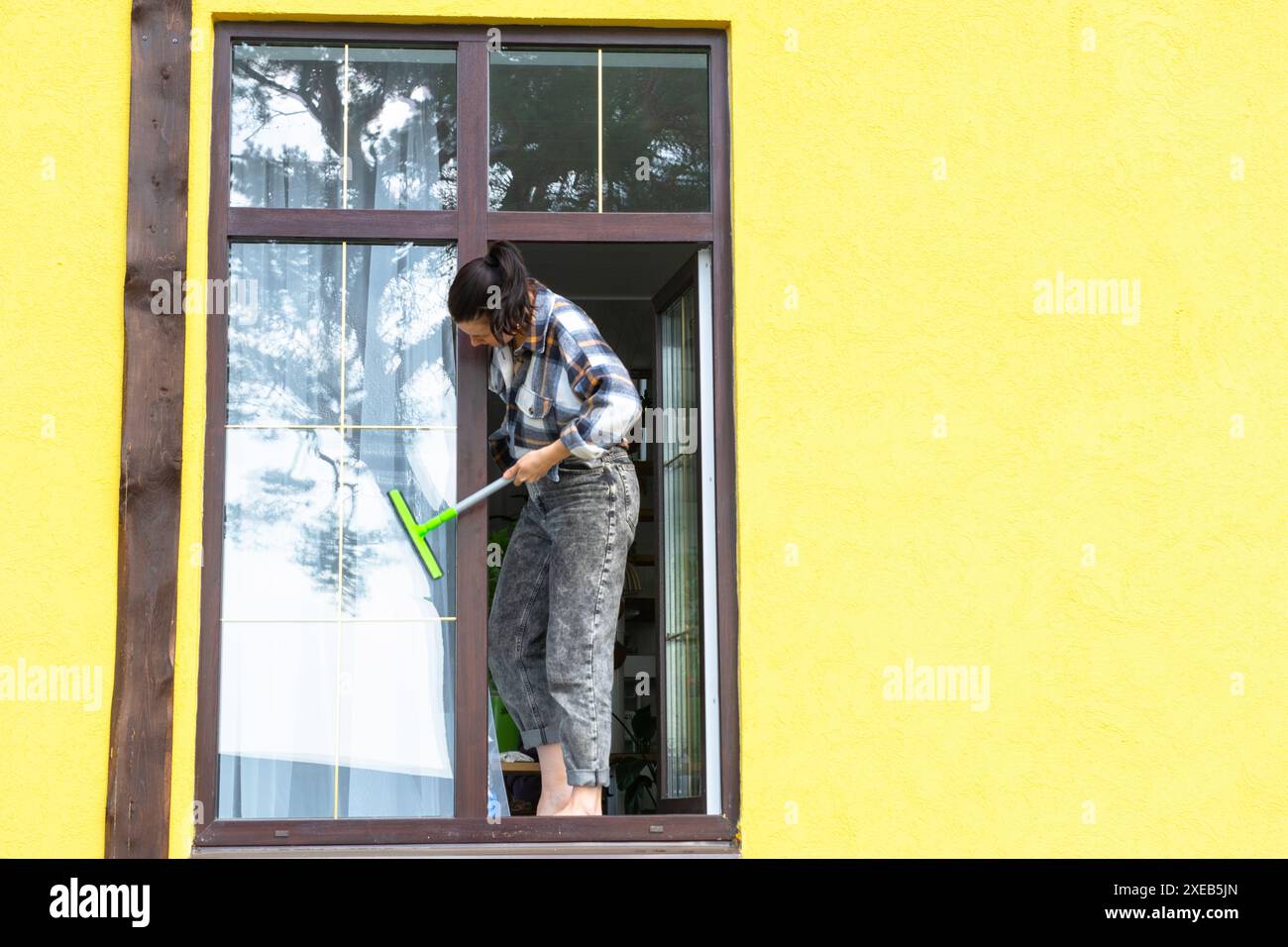 A woman manually washes the window of the house with a rag with a spray ...