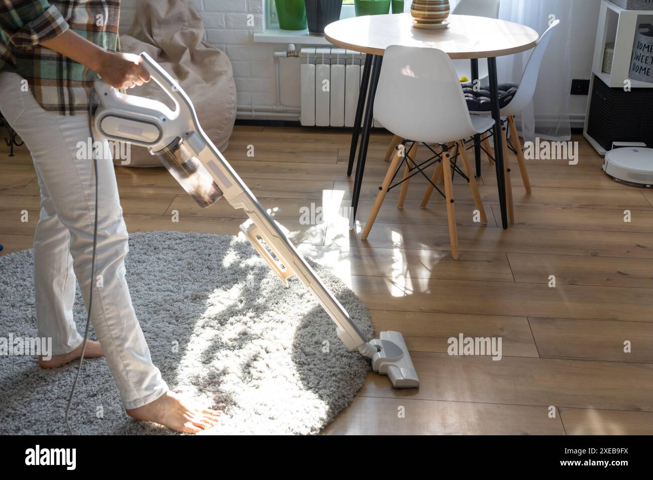 A woman vacuums a round carpet in a house among house plants with a ...