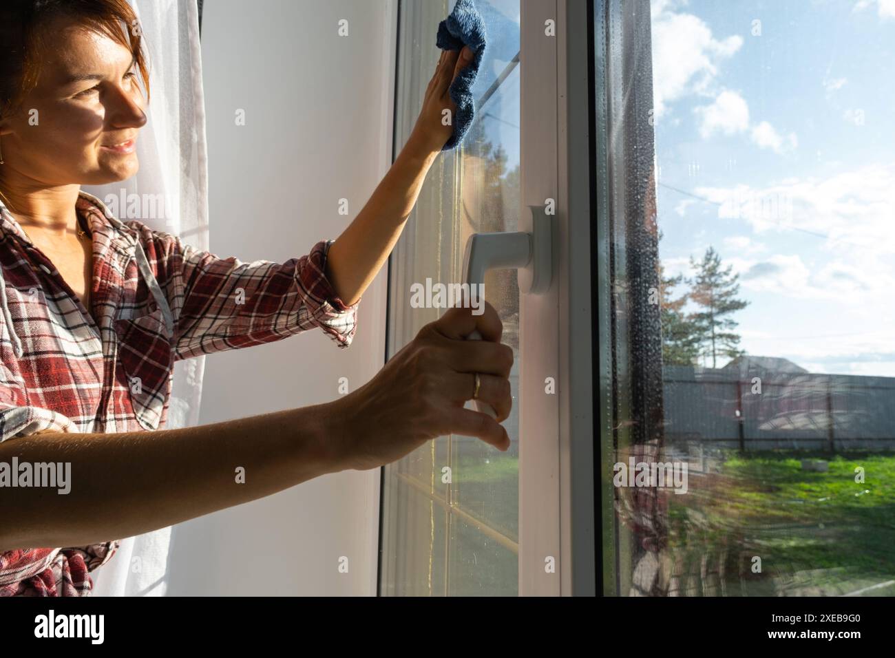 Woman manually washes the window of the house with a rag with spray ...
