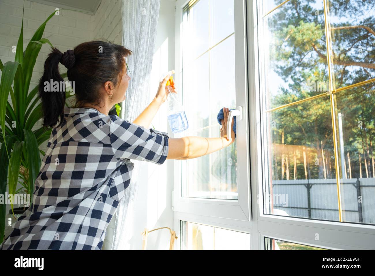 Woman manually washes the window of the house with a rag with spray ...