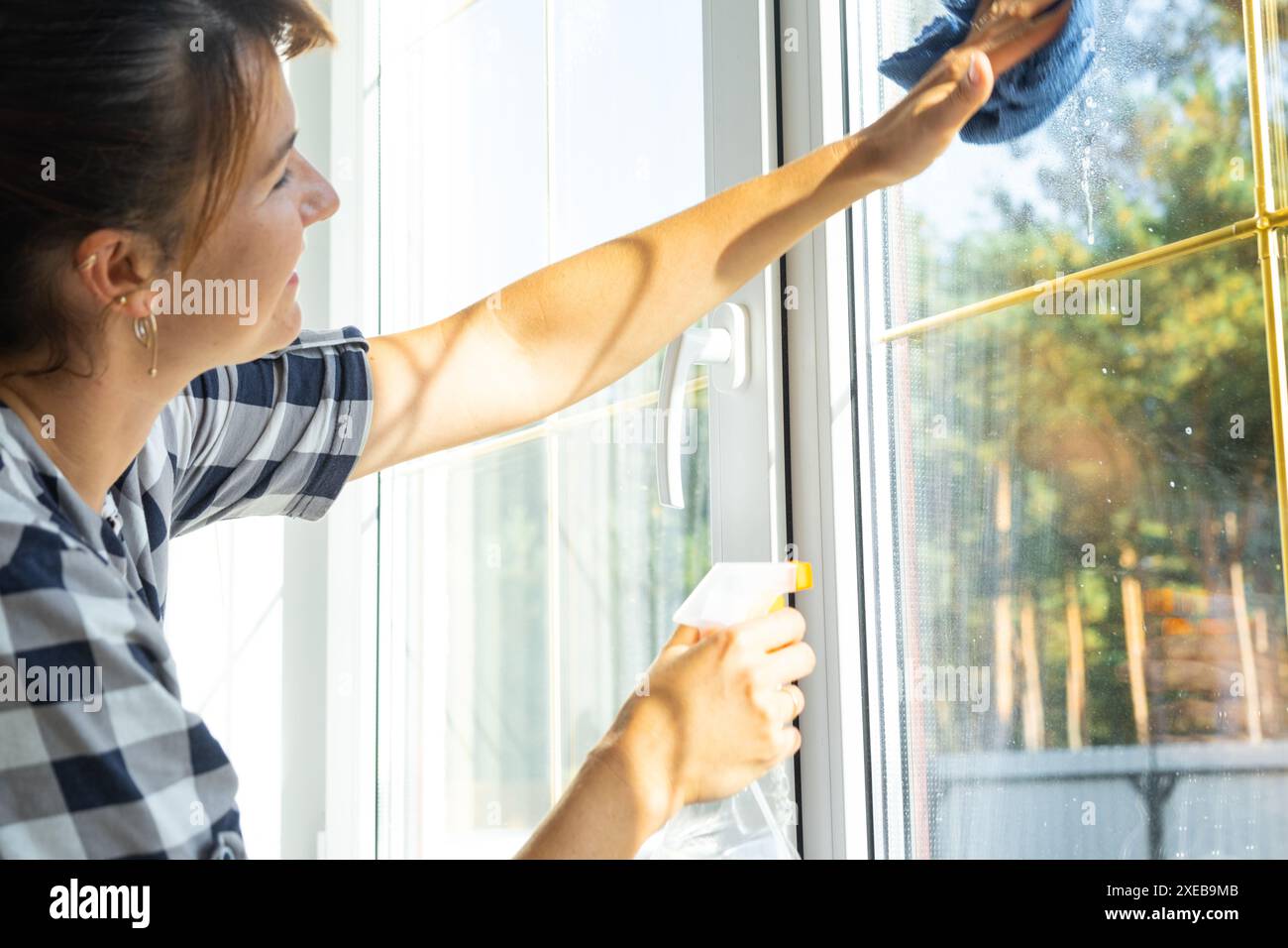 Woman manually washes the window of the house with a rag with spray ...