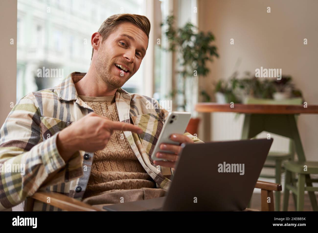 Excited guy in cafe, sitting with phone and pointing at screen with ...