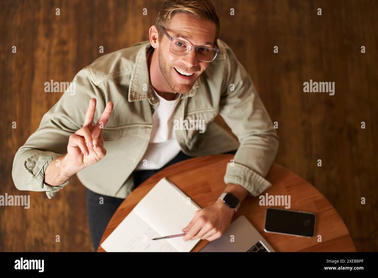 Upper angle shot of handsome smiling man in glasses, showing peace sign ...
