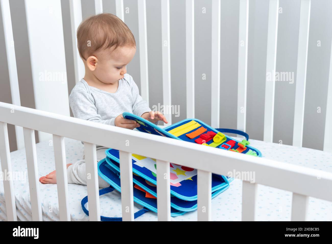 Baby playing with montessori busy book sitting in crib. Concept of ...
