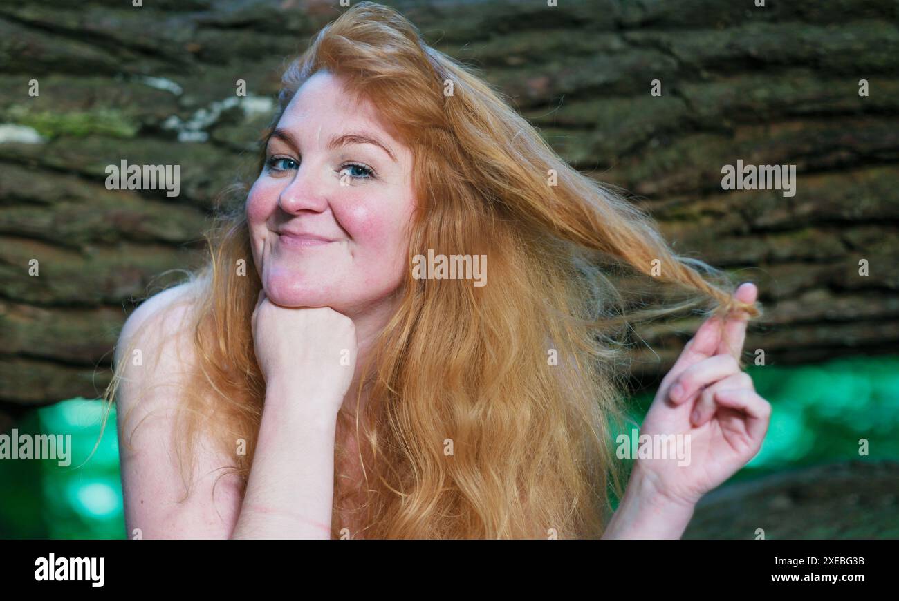 smiling woman with long, red hair sits outdoors, resting her chin on ...