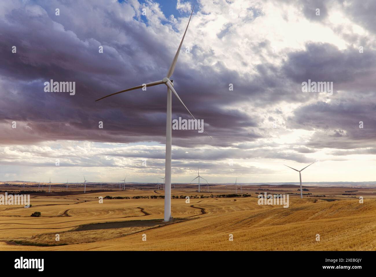 Dramatic sky over wind turbines in a vast, hilly agricultural landscape ...