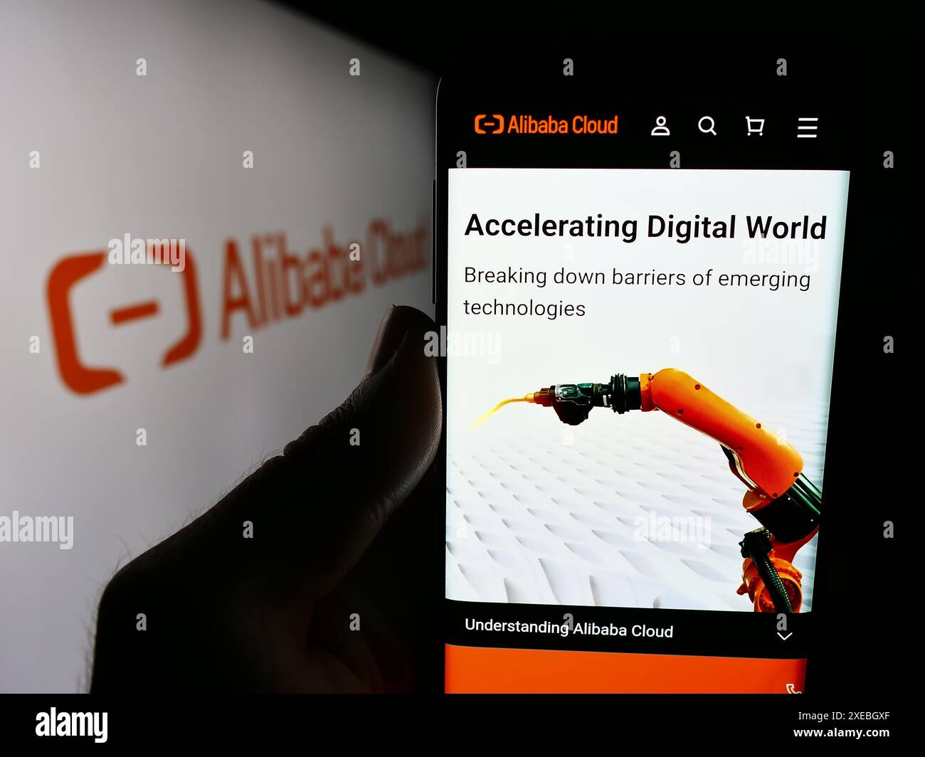 Person holding cellphone with webpage of Chinese computing company Alibaba Cloud in front of ...
