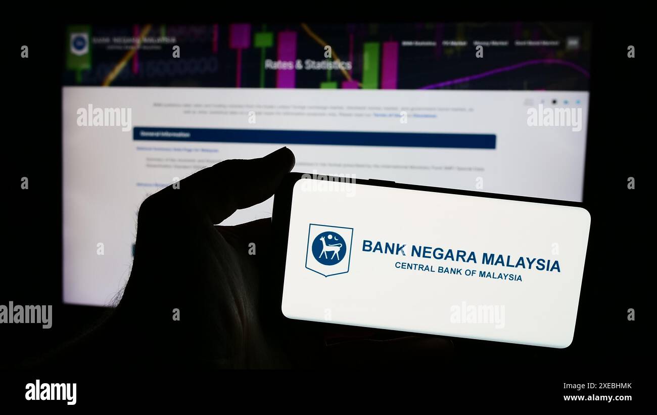 Person holding mobile phone with logo of Malaysian institution Bank ...