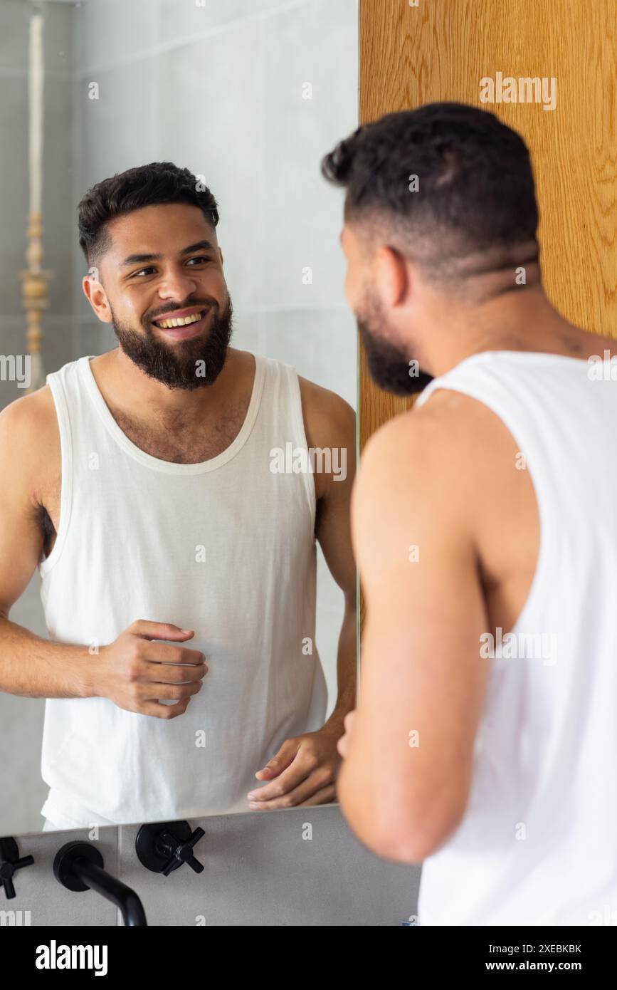At home, Man smiling at reflection in bathroom mirror, wearing white ...