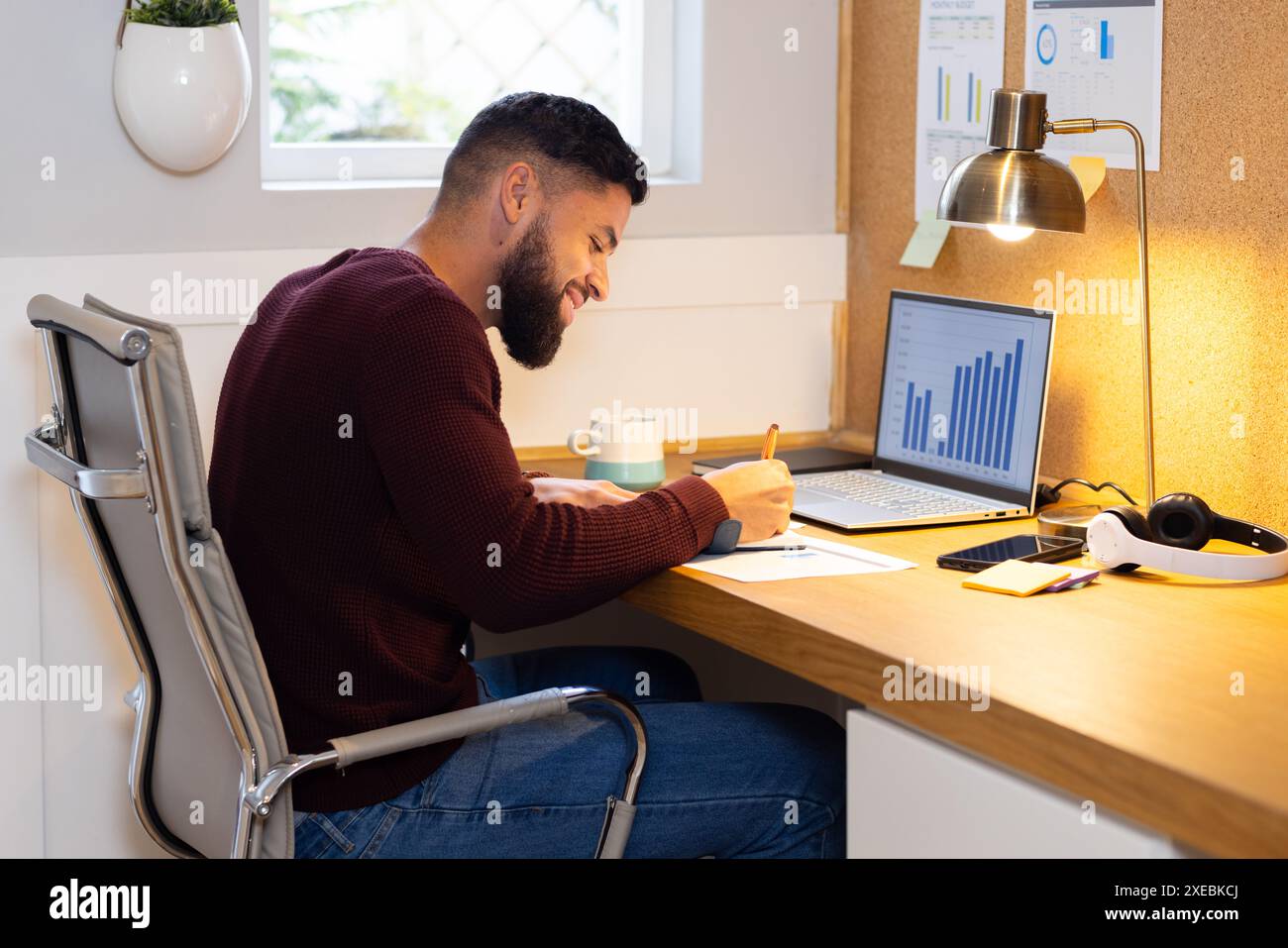 Working from home, man writing notes and using laptop with charts on ...