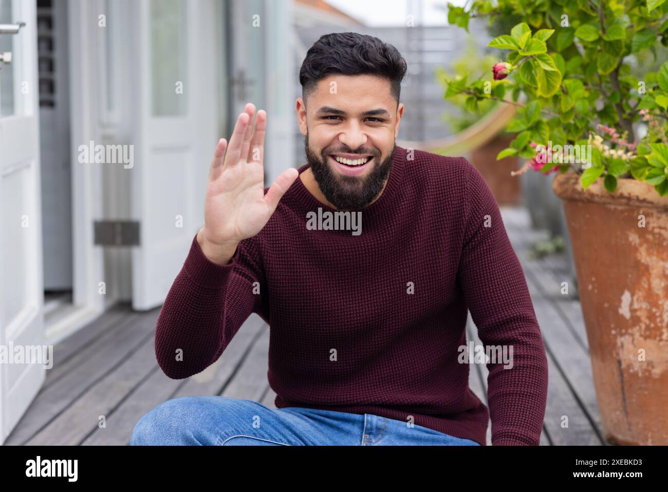 Smiling man waving hand while sitting on wooden deck at home, on video ...