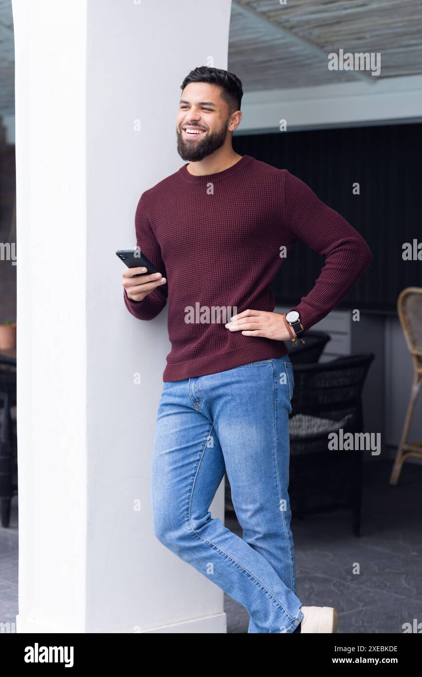 Outside his home, Smiling man holding smartphone and leaning against ...