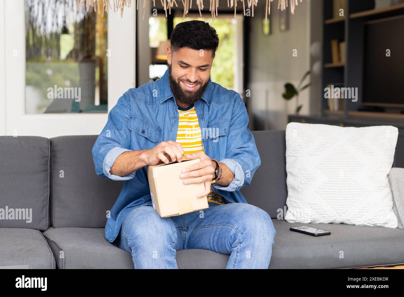 Man opening package while sitting on couch at home, smiling happily ...