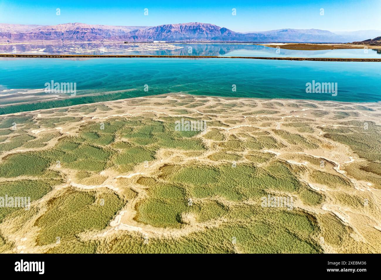 Dead Sea. The green water of the salty sea is surrounded by pink mountains. Salt deposits are ...