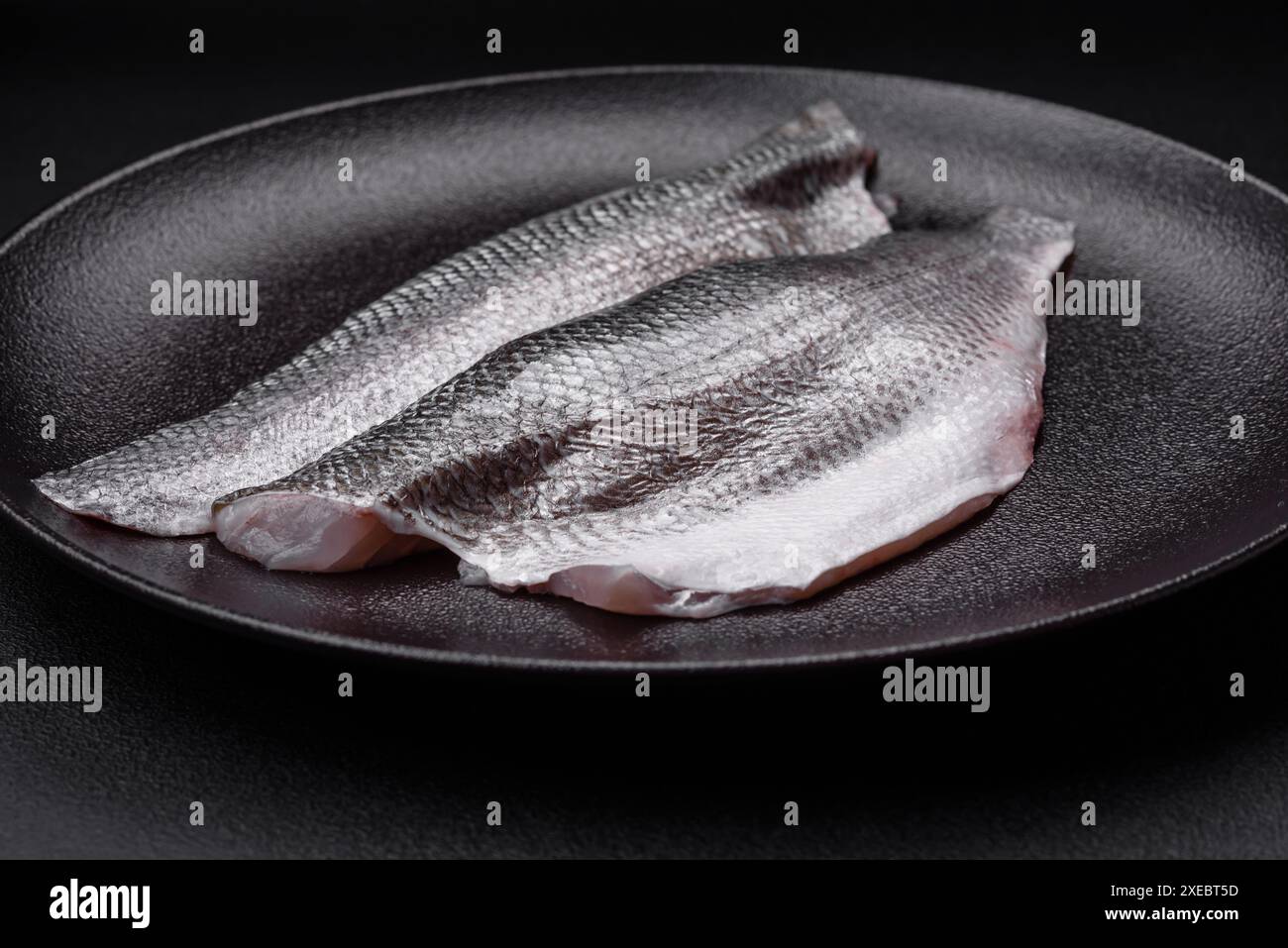 Raw sea bass fish fillet with salt, spices and herbs on a ceramic plate ...