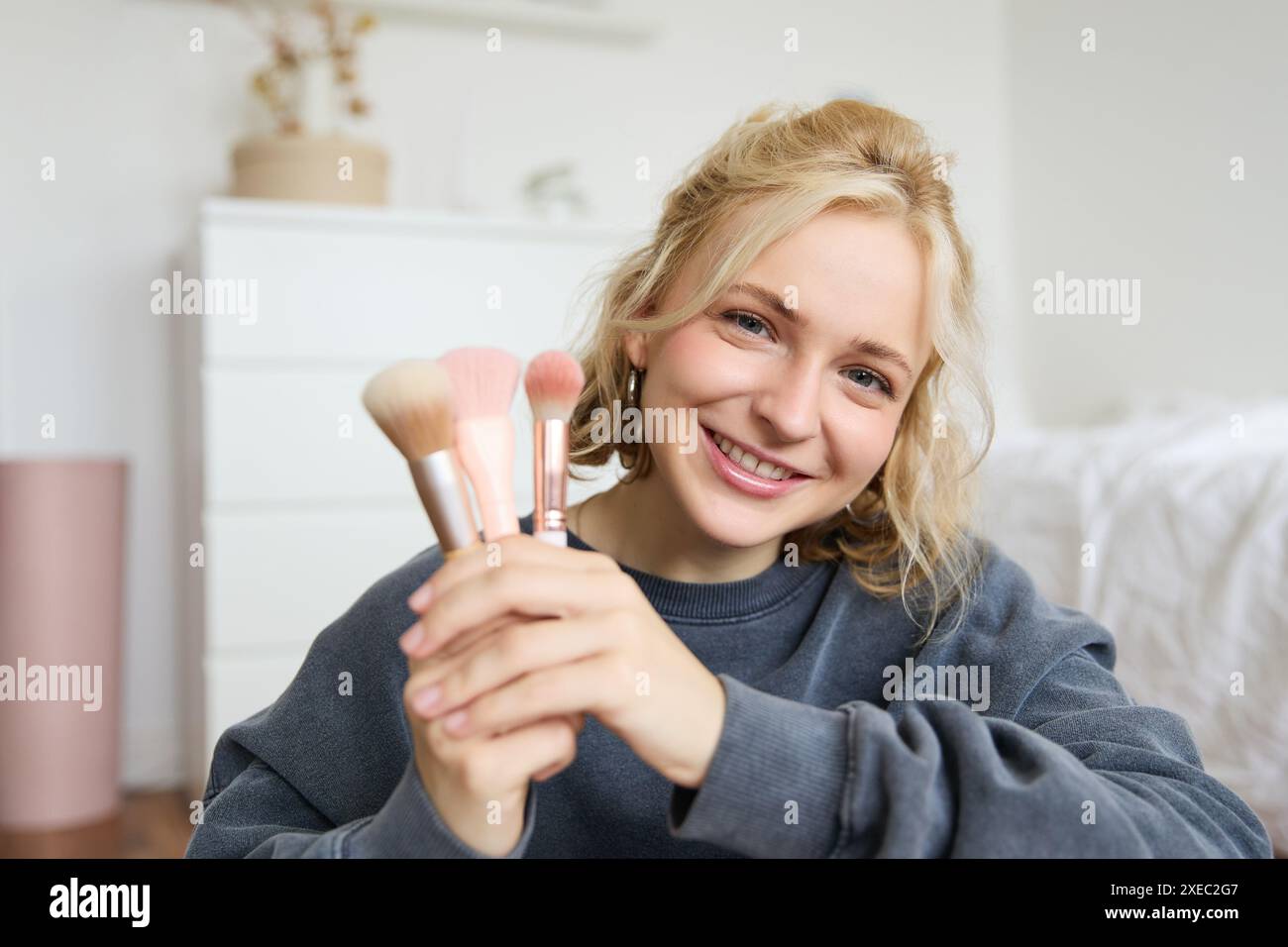 Close up portrait of cute teen girl showing her beauty makeup brushes, smiling and looking at ...